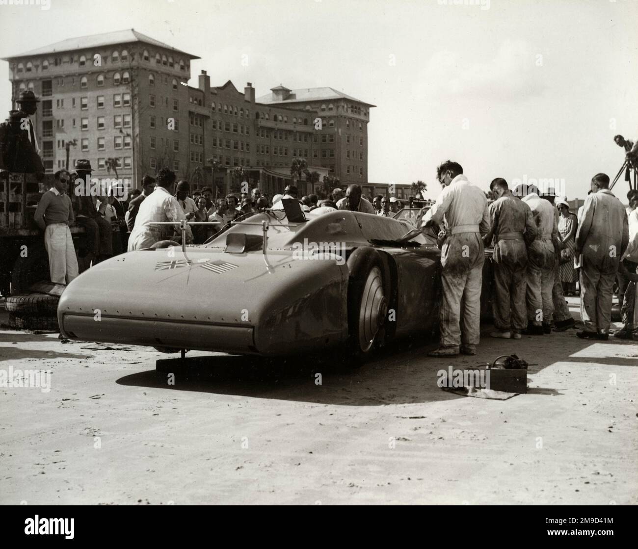 Mechanics working on Blue Bird in front of large hotel with crowds ...