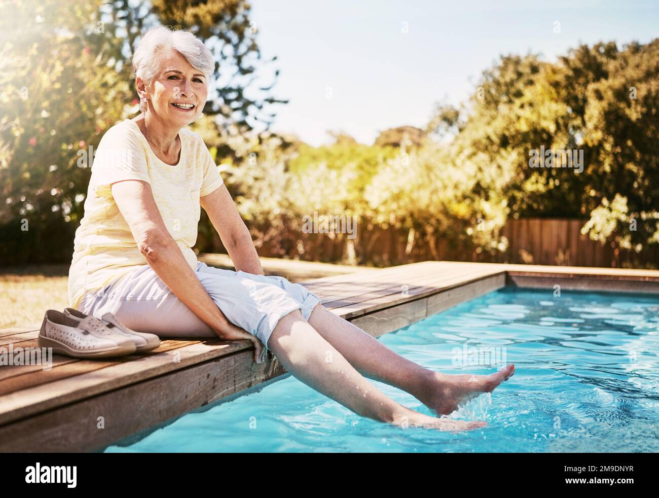 Senior woman with her feet in the pool while on a vacation, adventure ...