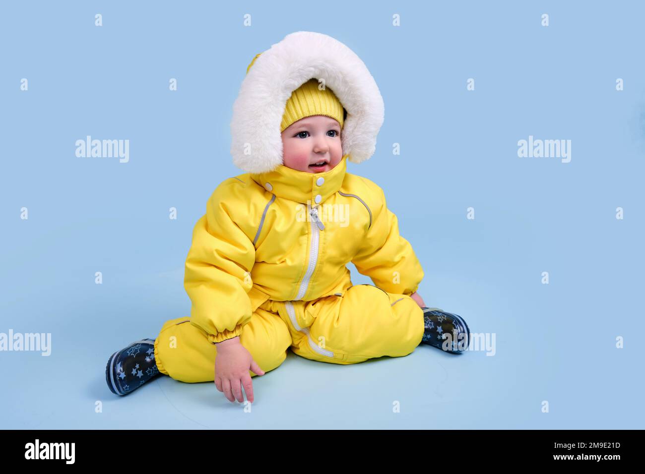 Happy toddler baby in winter clothes snowsuit on studio blue background ...