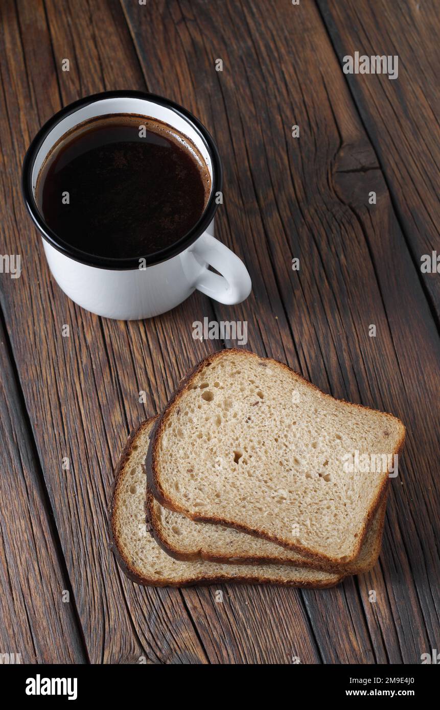 Pieces of bread and enameled cup of coffee on wooden table. High angle ...