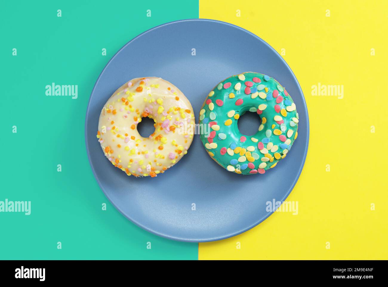 Two tasty donuts with icing and sprinkles on a plate on colored ...
