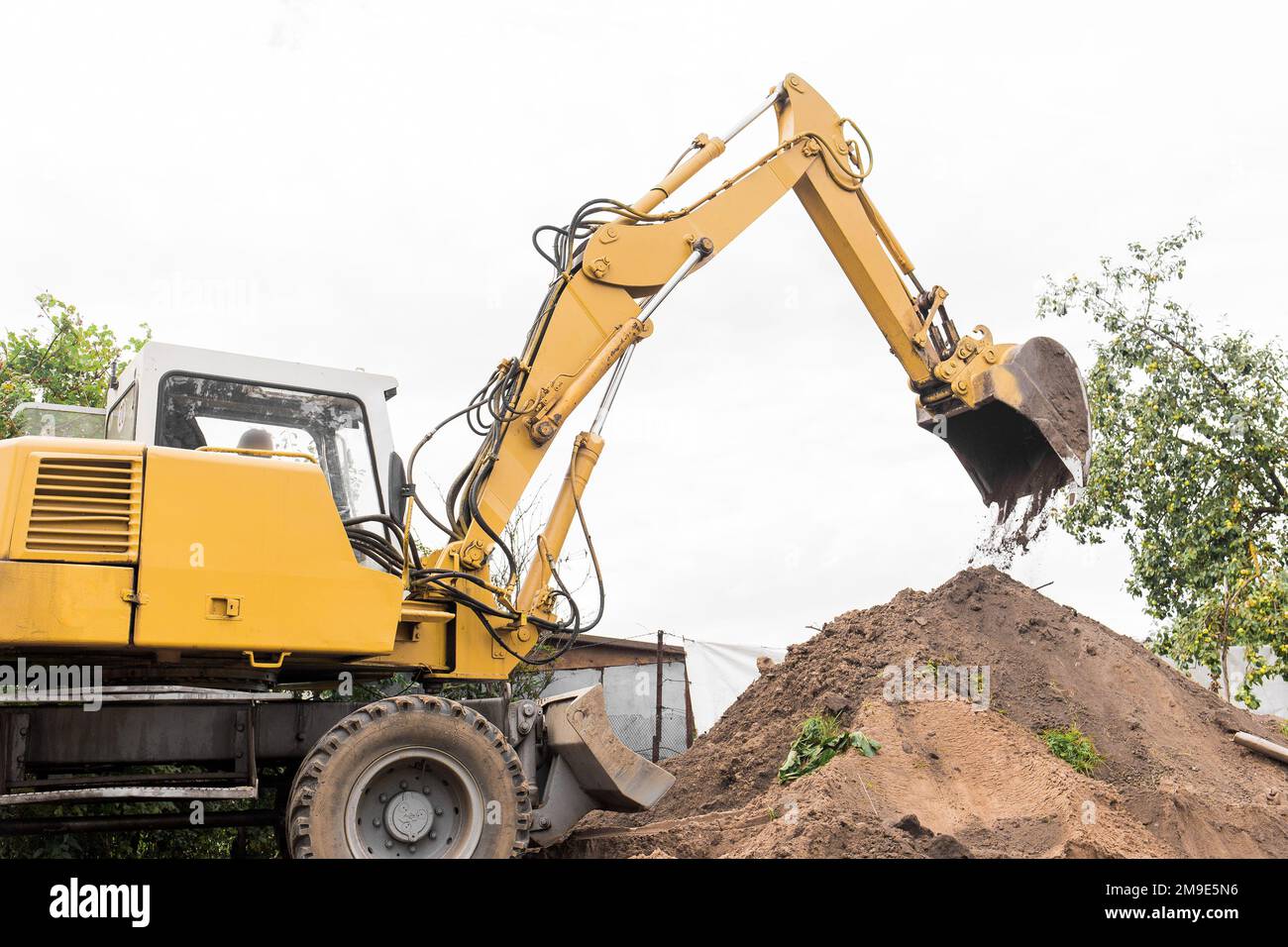 A hydraulic piston and a bucket excavator dig the ground next to a pile ...