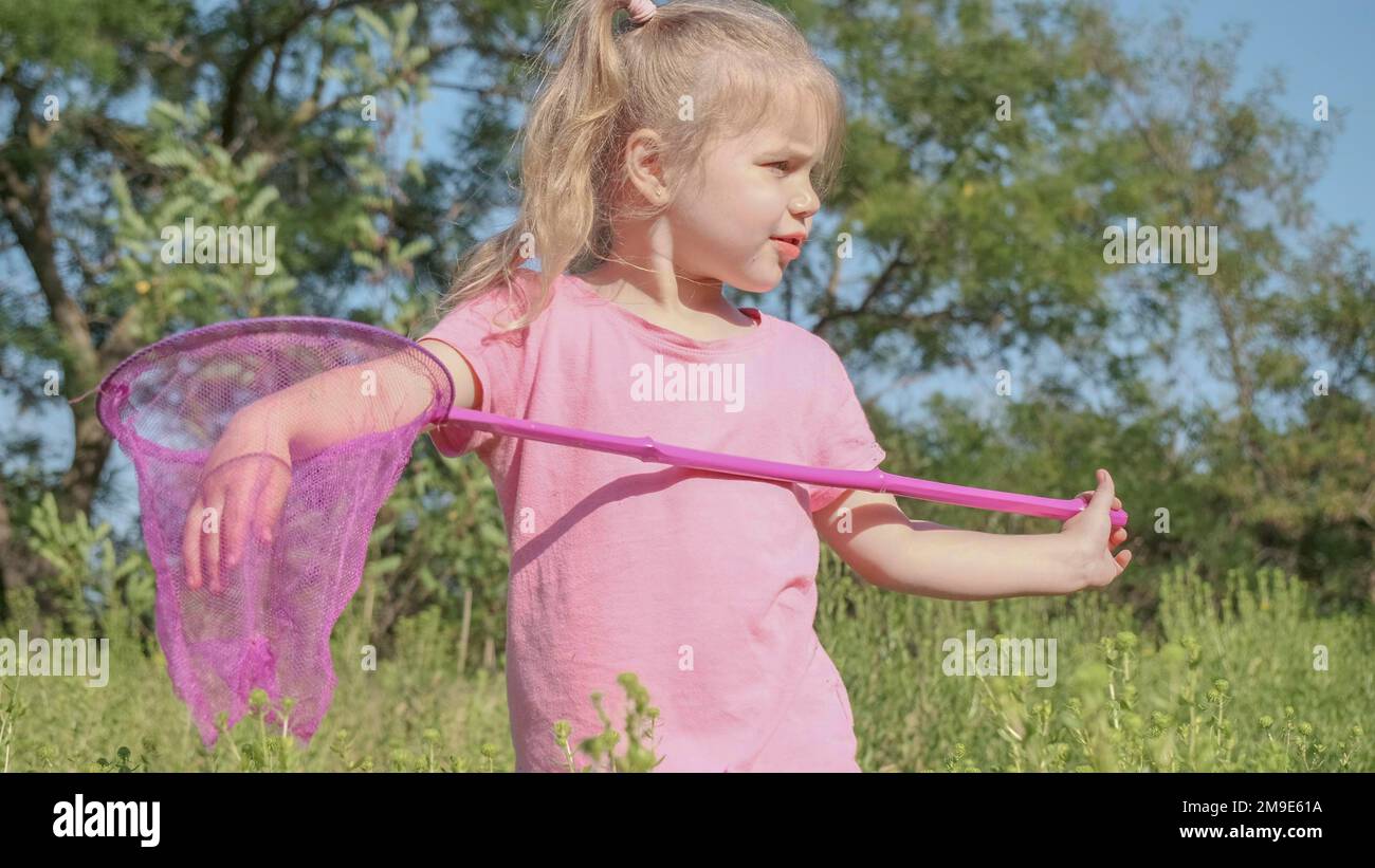 Little girl plays with butterfly net of tall grass in city park. Cute ...