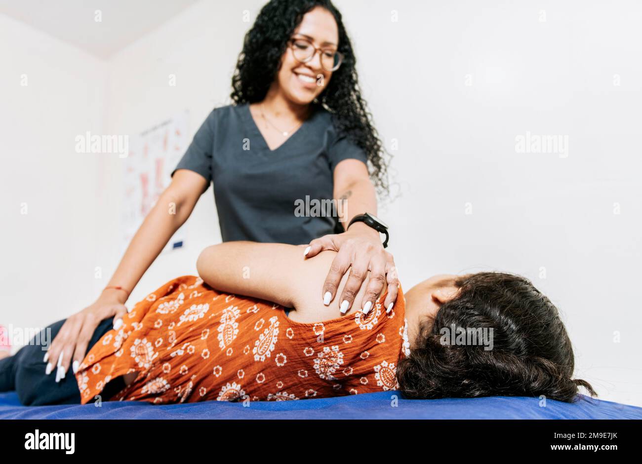 Physiotherapist rehabilitating shoulder to patient lying on her side. Shoulder and back ...