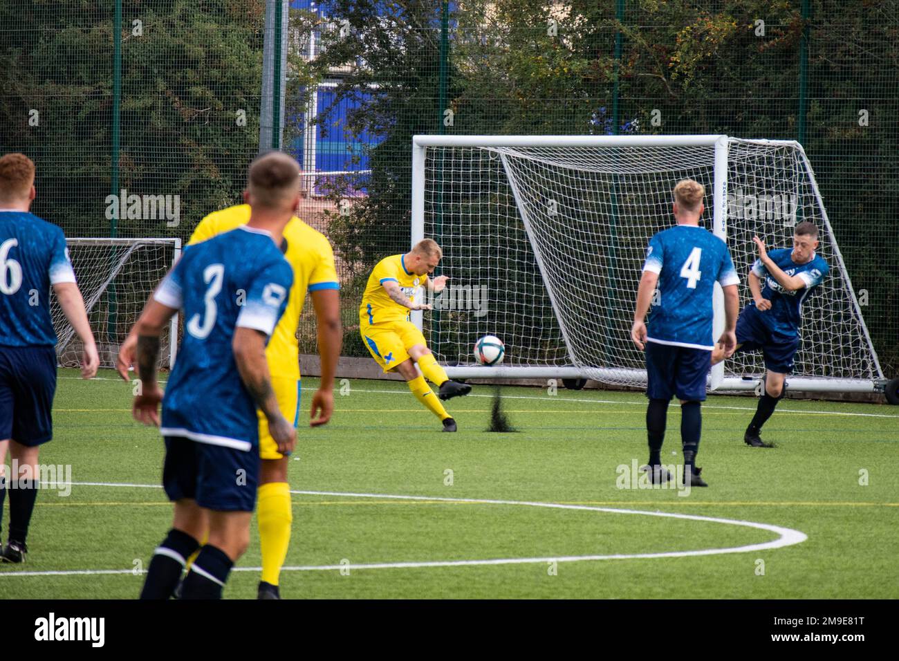 A soccer player in yellow kit taking a free kick against blue team ...