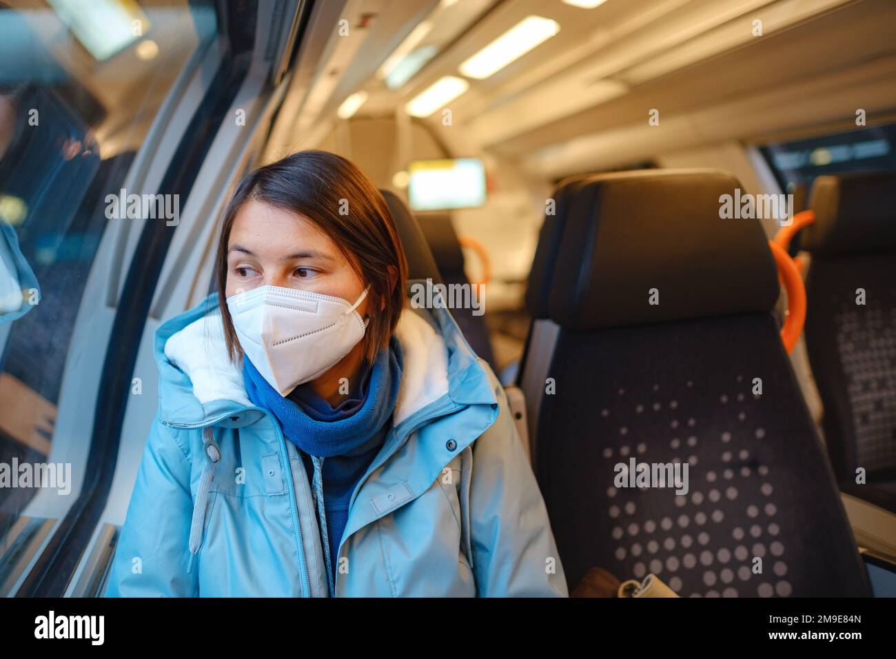 Asian Woman in blue jacket and protective mask looking out of train ...