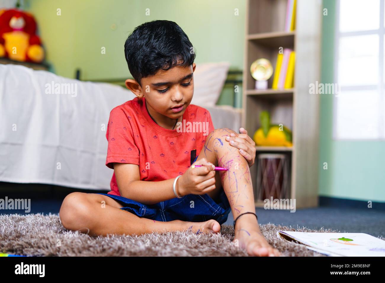 Preteen playful kid making drawings on leg using sketch pens at home ...