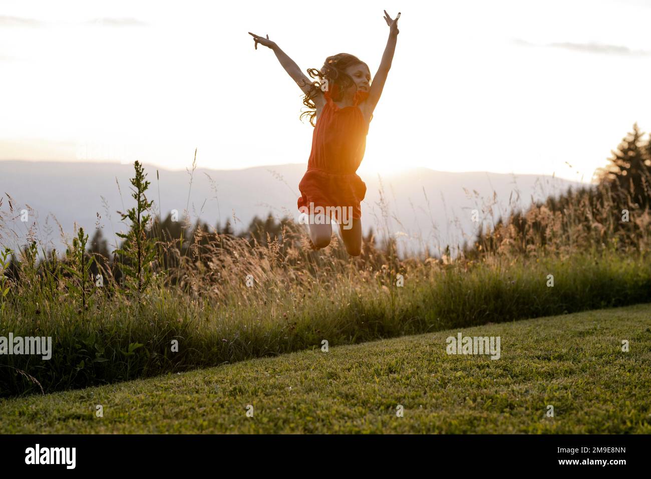 Girl, 8 years, jumping in a meadow at sunset, Carinthia, Austria Stock ...
