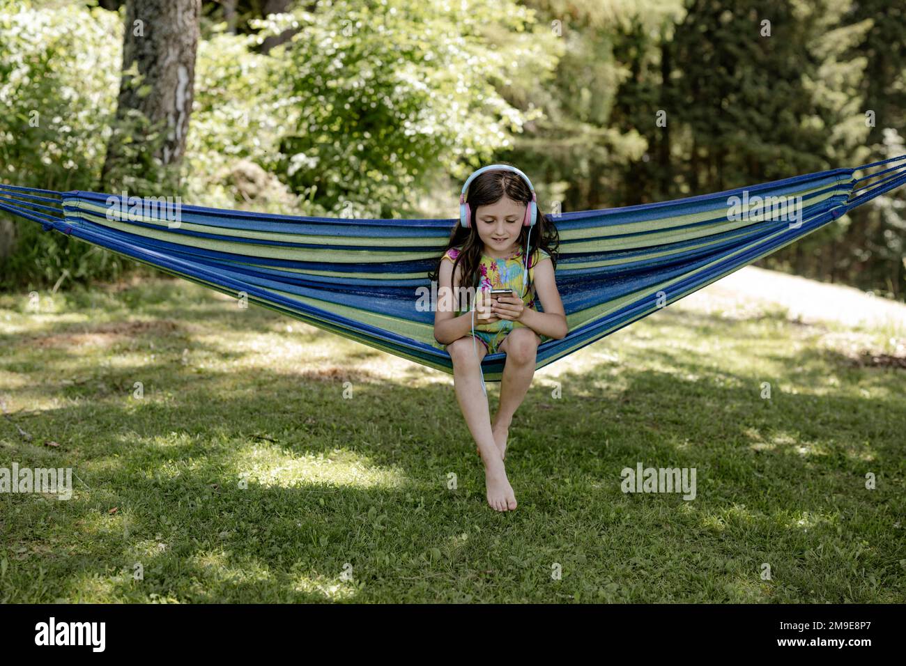 Girl, 8 years, sitting in a hammock in the shade and listening to music ...