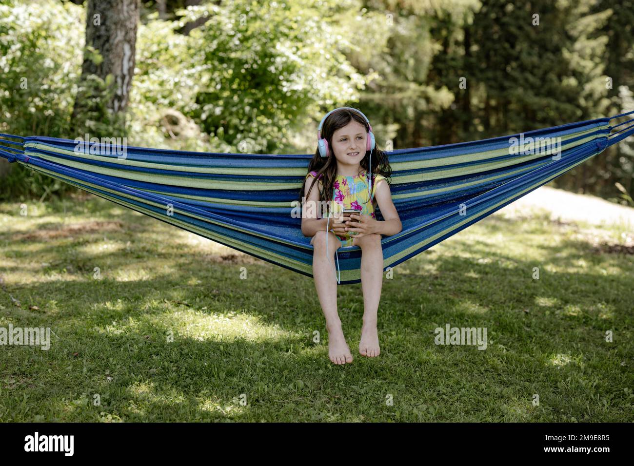 Girl, 8 years, sitting in a hammock in the shade and listening to music ...