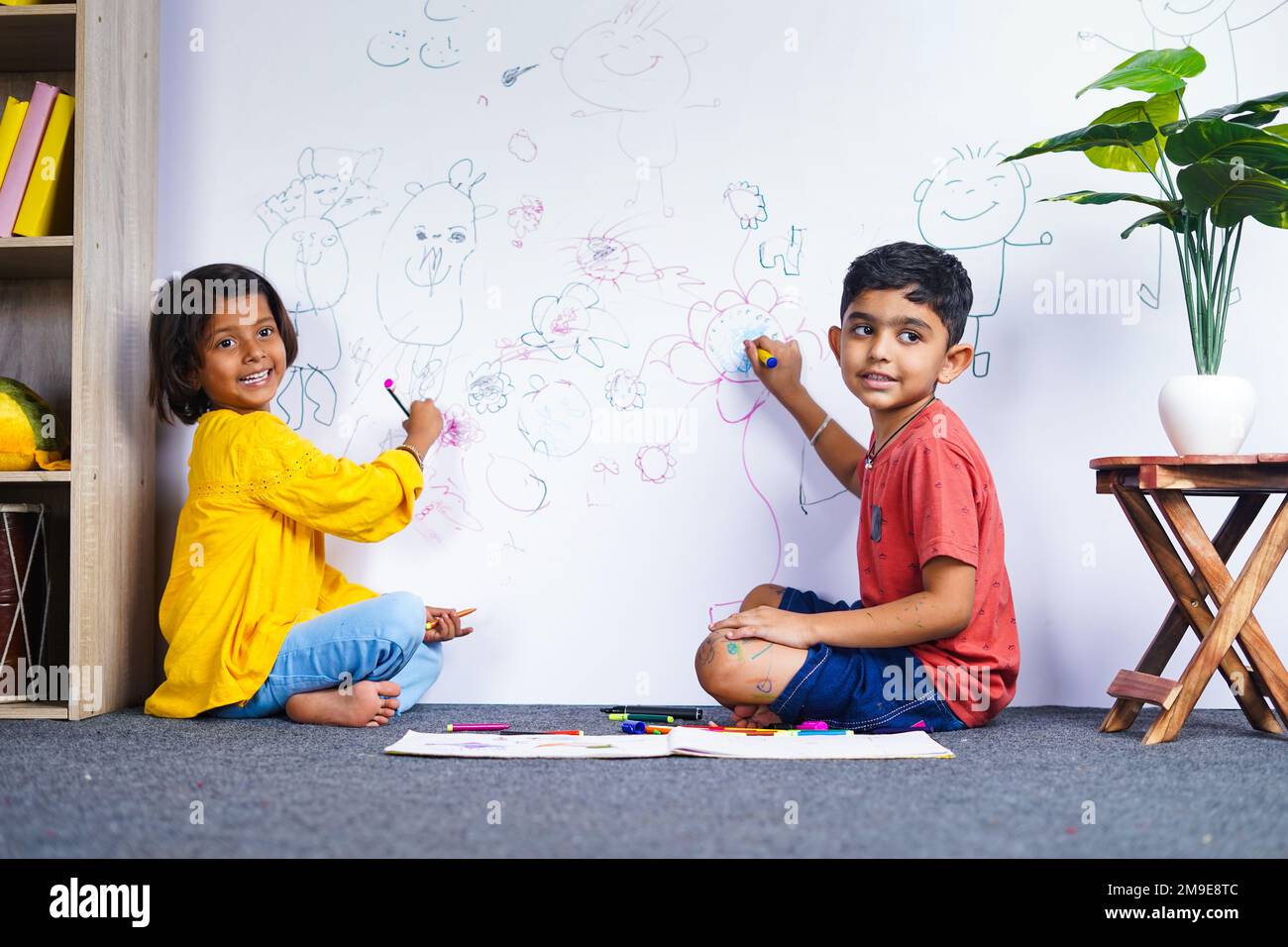 Young siblings kids drawing with crayon color on wall by looking at ...