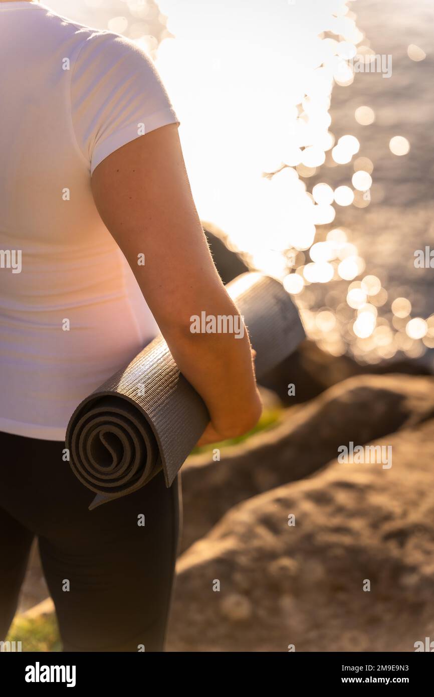 Hands of a woman with the yoga mat in nature by the sea at sunset ...