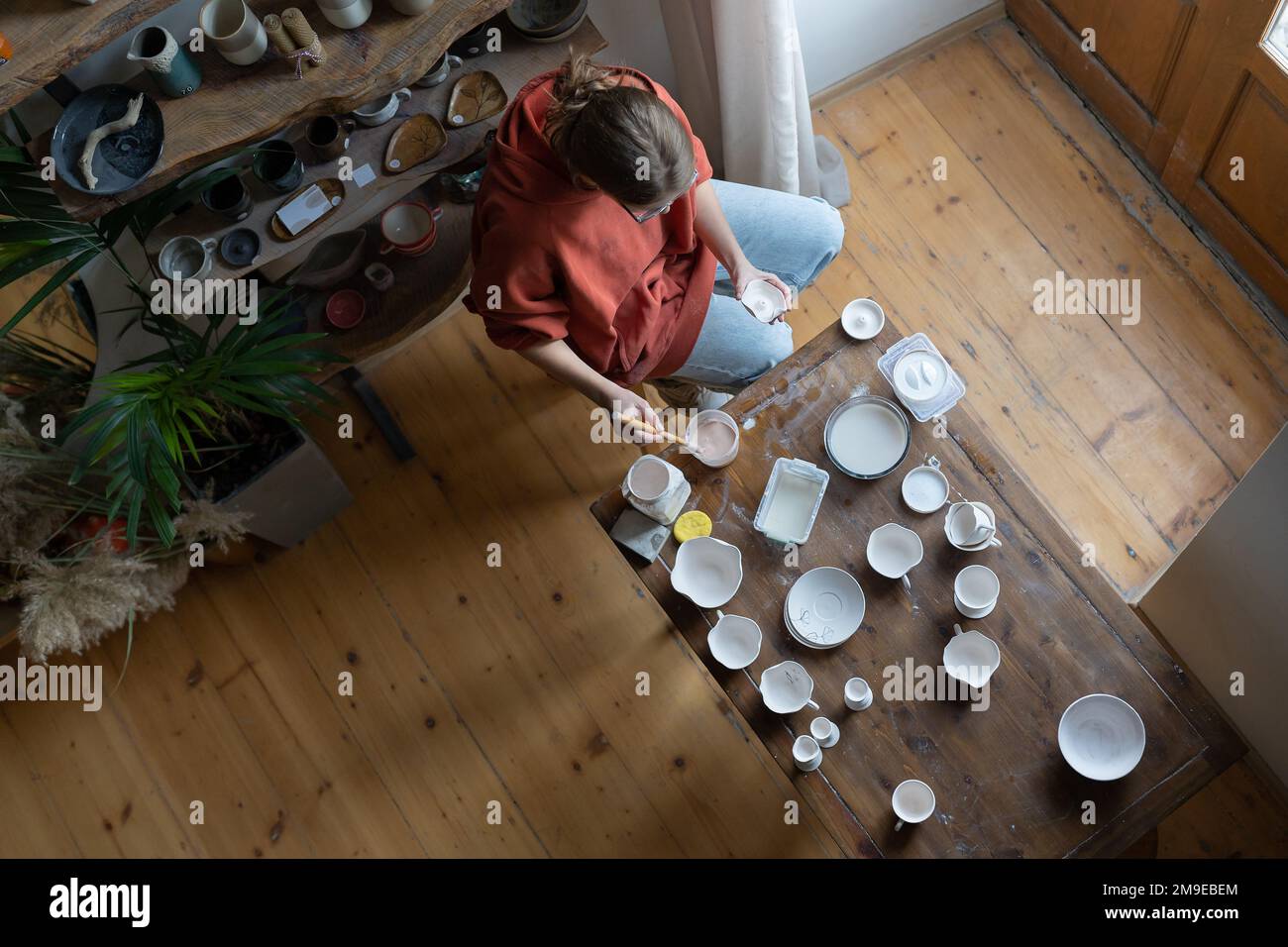 Top view of pottery workshop. Woman craftsman paints ceramic dishes for ...