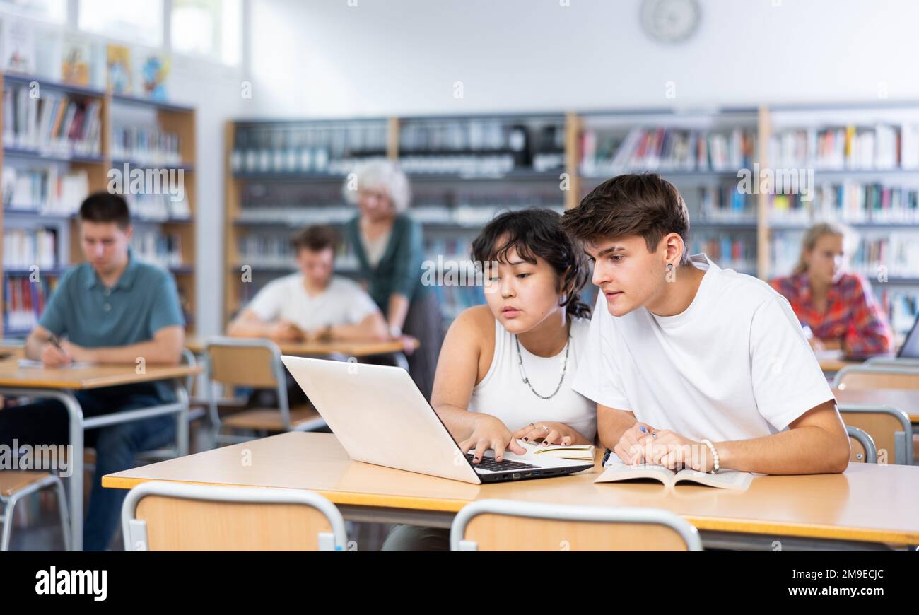 Boy and girl study together at laptop while sitting in school library ...