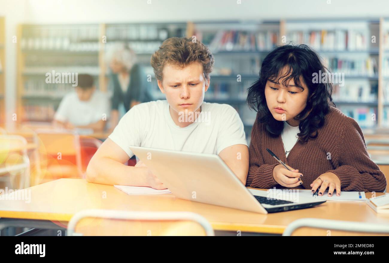 Boy and girl study together at laptop while sitting in school library ...