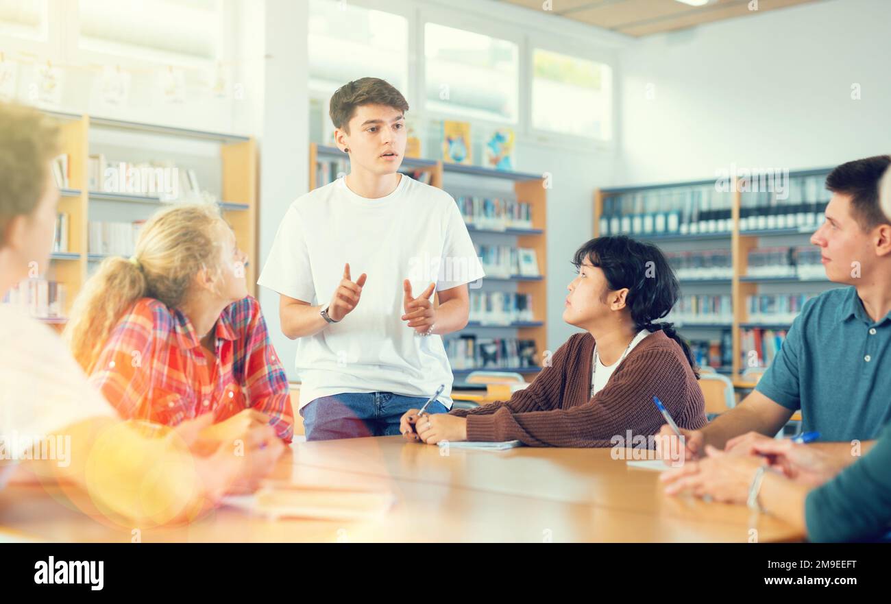 Positive teenage male student giving report during group lesson in ...