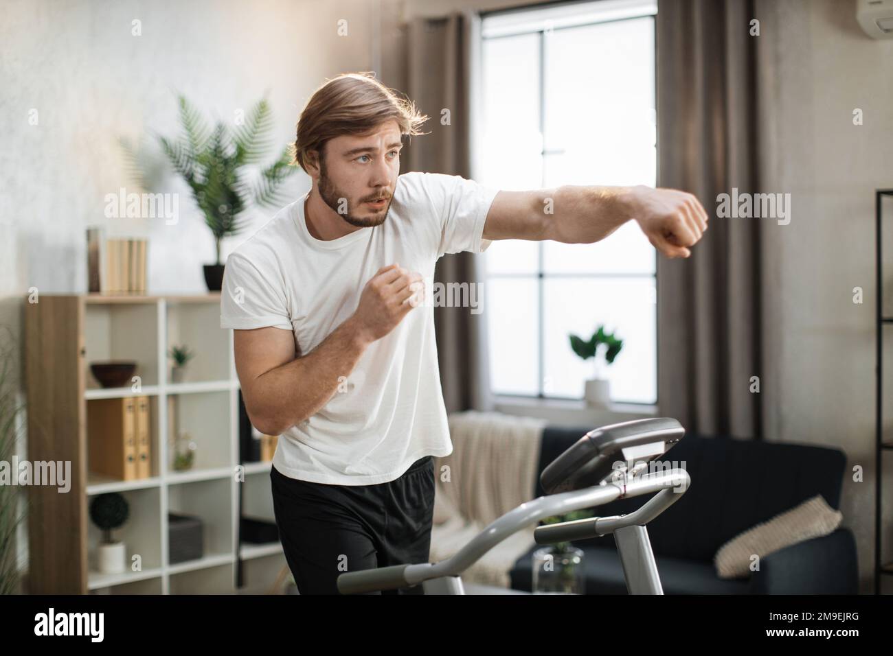 Young attractive sporty man in white t-shirt doing boxing punches while ...
