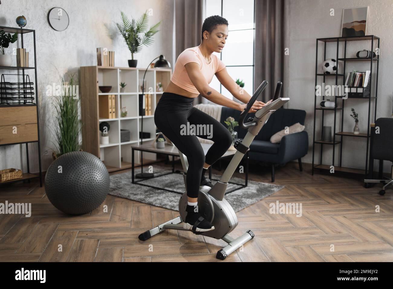 African smiling young sportswoman doing cardio on stationary bike ...