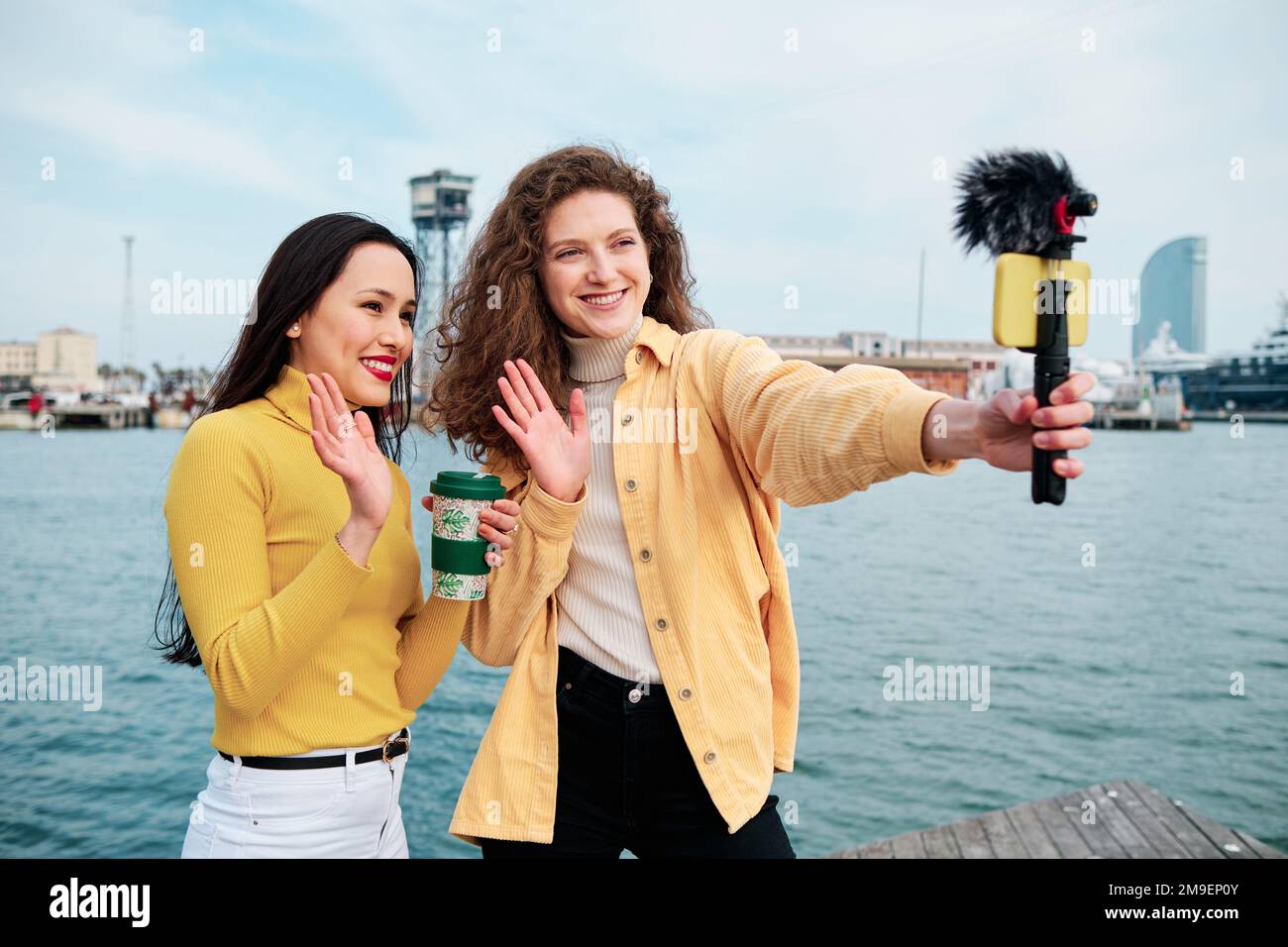 Two women smiling and waving hand while streaming live with a mobile ...