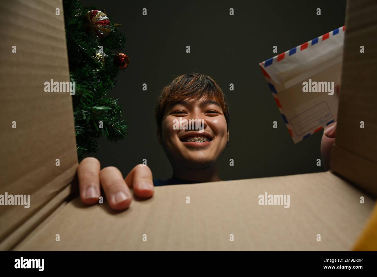Smiling young asian man holding greeting card looking inside cardboard ...
