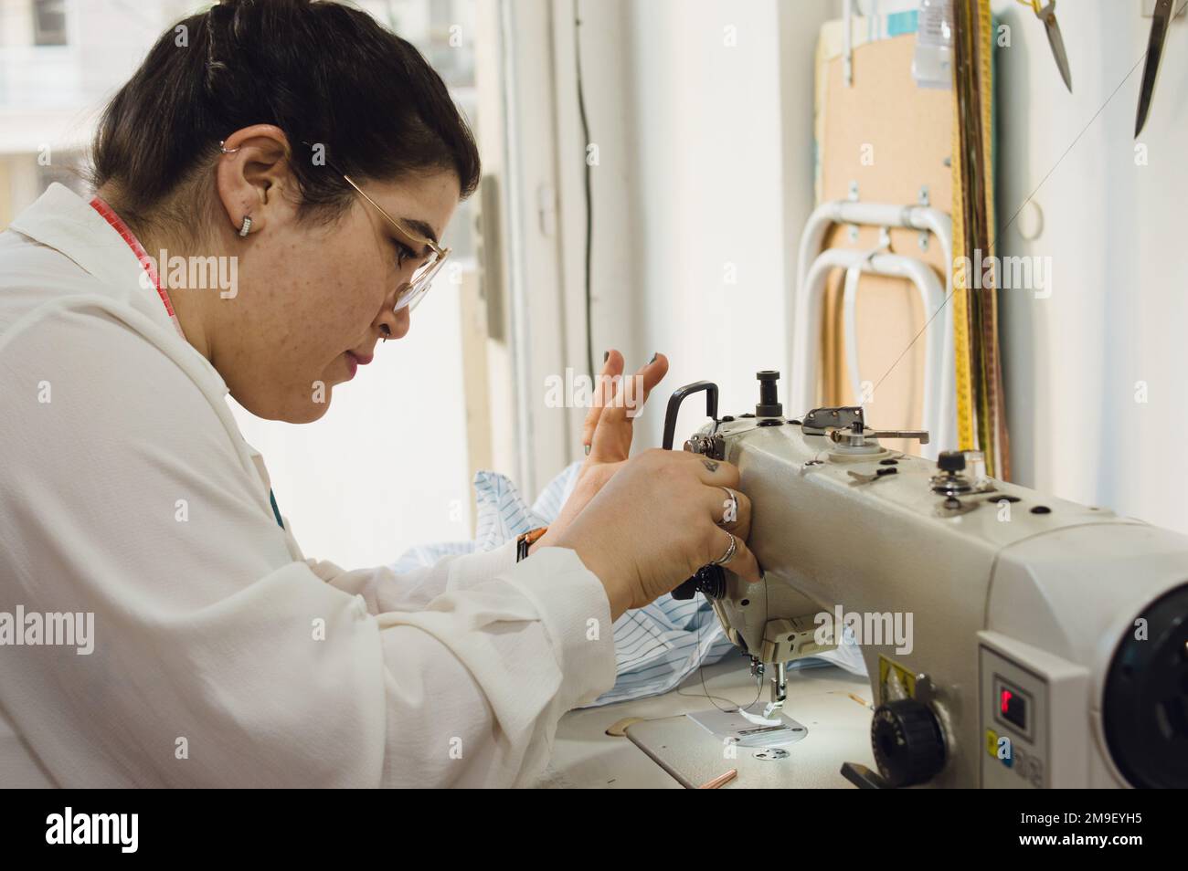 young caucasian woman with glasses seamstress, sitting in her sewing ...