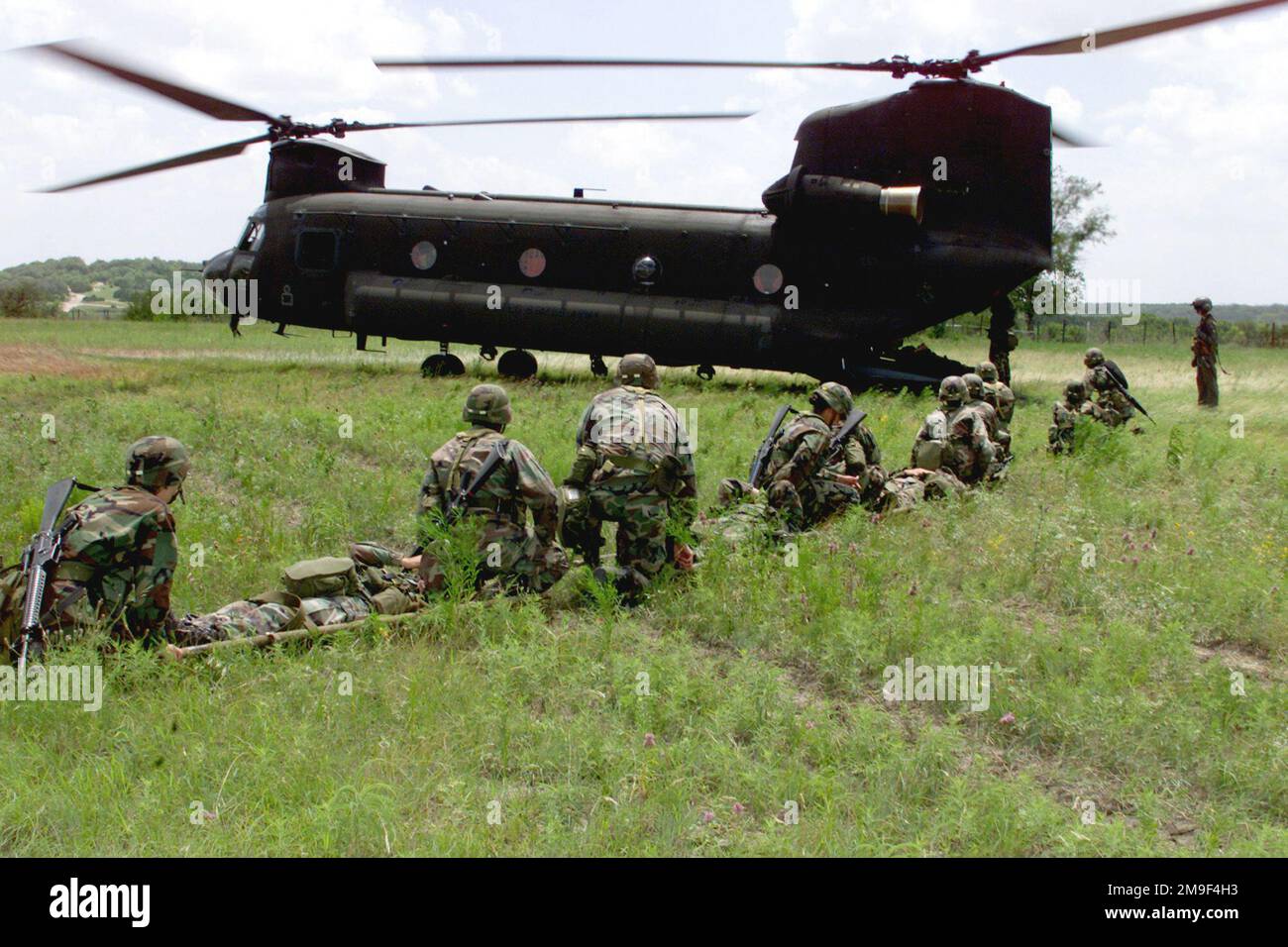A CH-47 Chinook idles on a grassy field with its engines running as ...