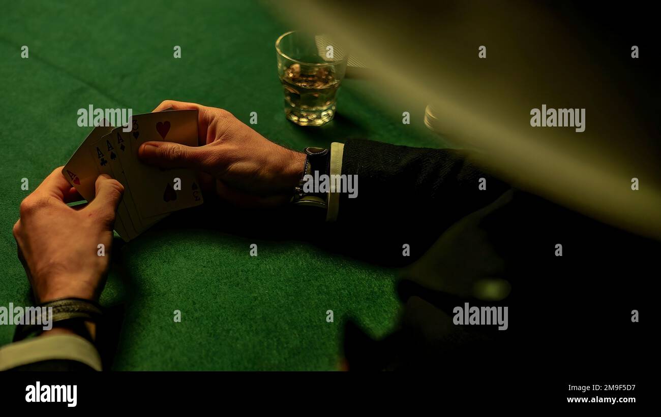 Hands closeup holding poker cards, with a whiskey glass and poker chips ...