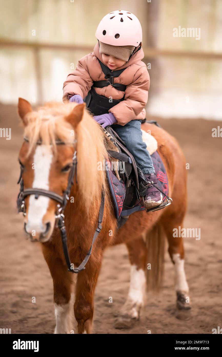 Little Child Riding Lesson. Three-year-old girl rides a pony and does ...