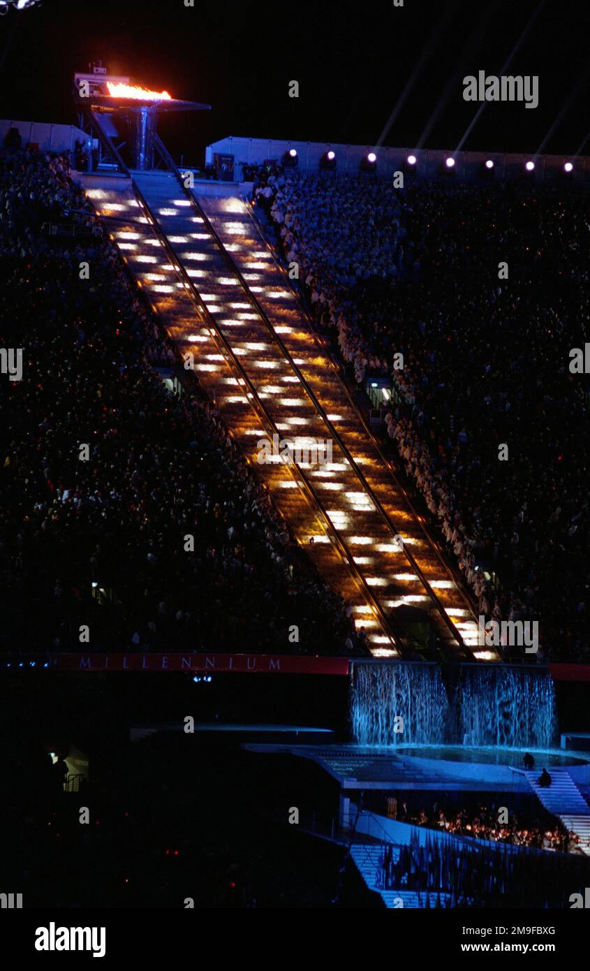 The Olympic torch is lit while raised to the top of the Olympic Stadium ...