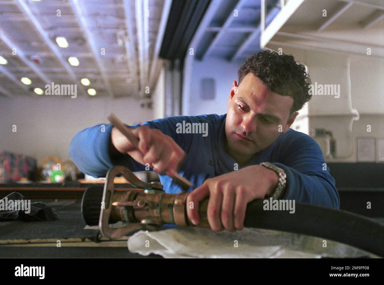 US Navy AIRMAN Edwin Sanchez cleans a fire hose nozzle in the Hangar ...