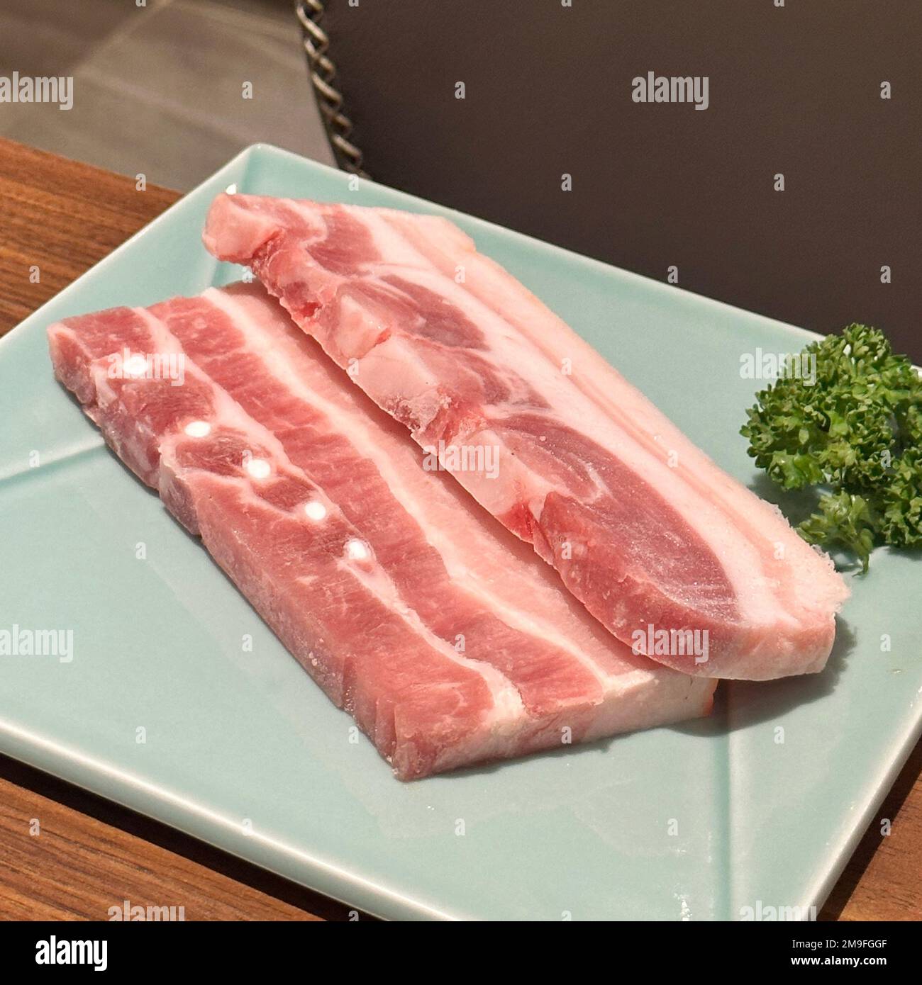 Grilling pork belly meat on a round iron BBQ net in restaurant for ...