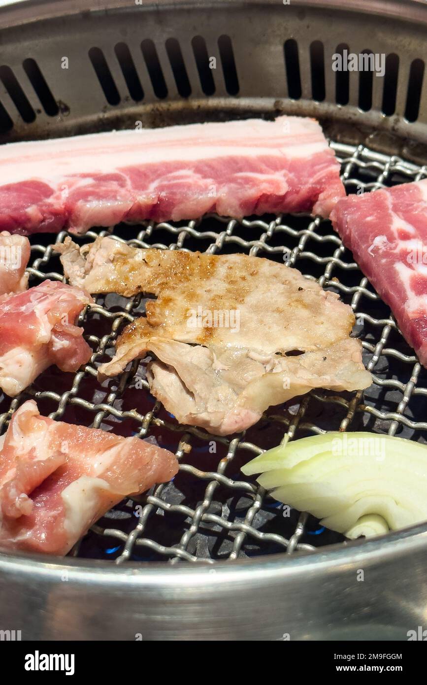 Grilling pork belly meat on a round iron BBQ net in restaurant for ...