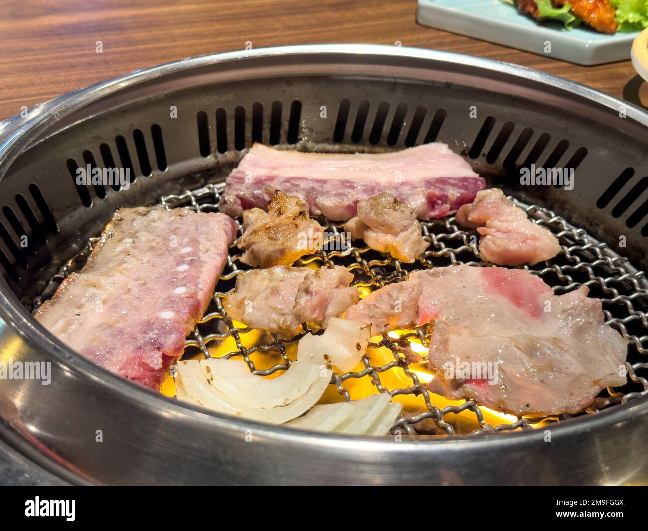 Grilling pork belly meat on a round iron BBQ net in restaurant for ...