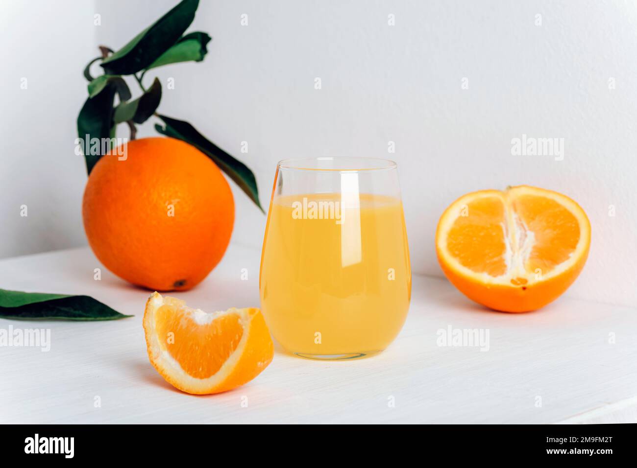 A glass of orange juice and orange fruits on white table. Front view ...