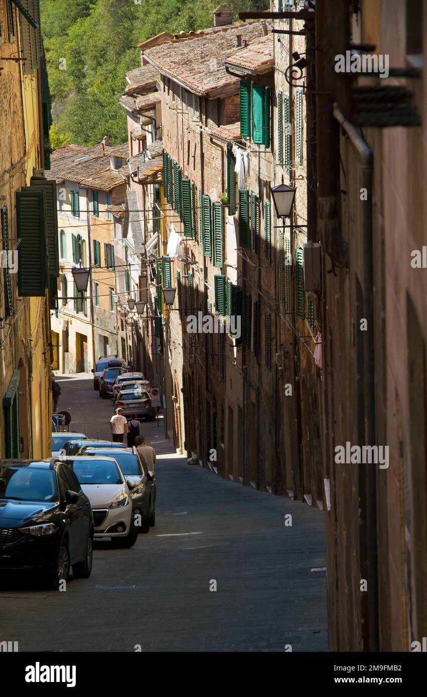 Downhill narrow street in Tuscany, partly shaded, sun in the distance ...