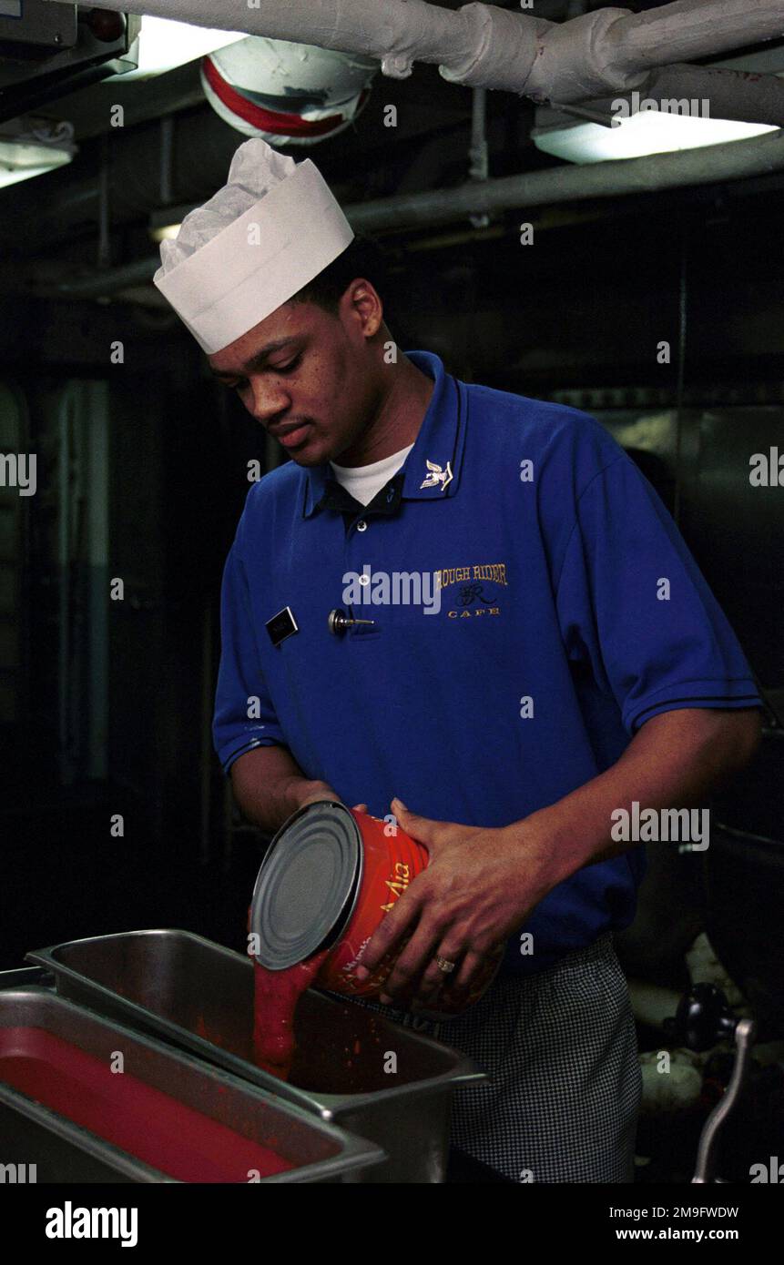 Mess SPECIALIST 3rd Class Ken Thomas pours tomato sauce into a chili ...