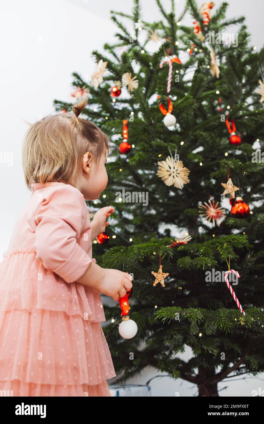 Low angle view, baby girl in pink dress looking up at the Christmas ...