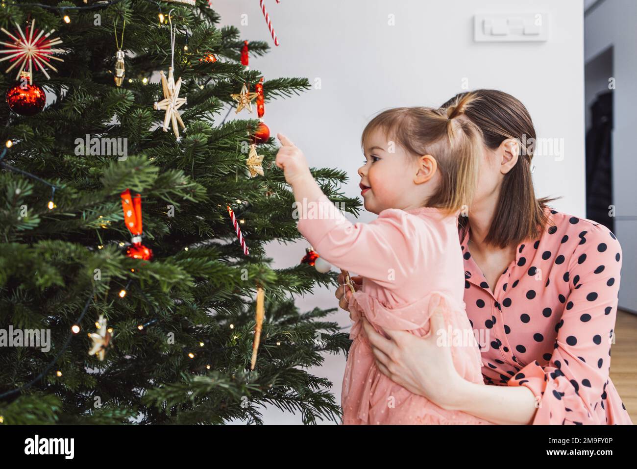 Mom and baby girl decorating the Christmas tree, putting on the ...