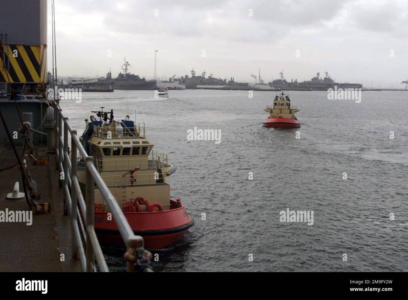 USS Anchorage (LSD-36) is assisted by tug boats while pulling out of ...