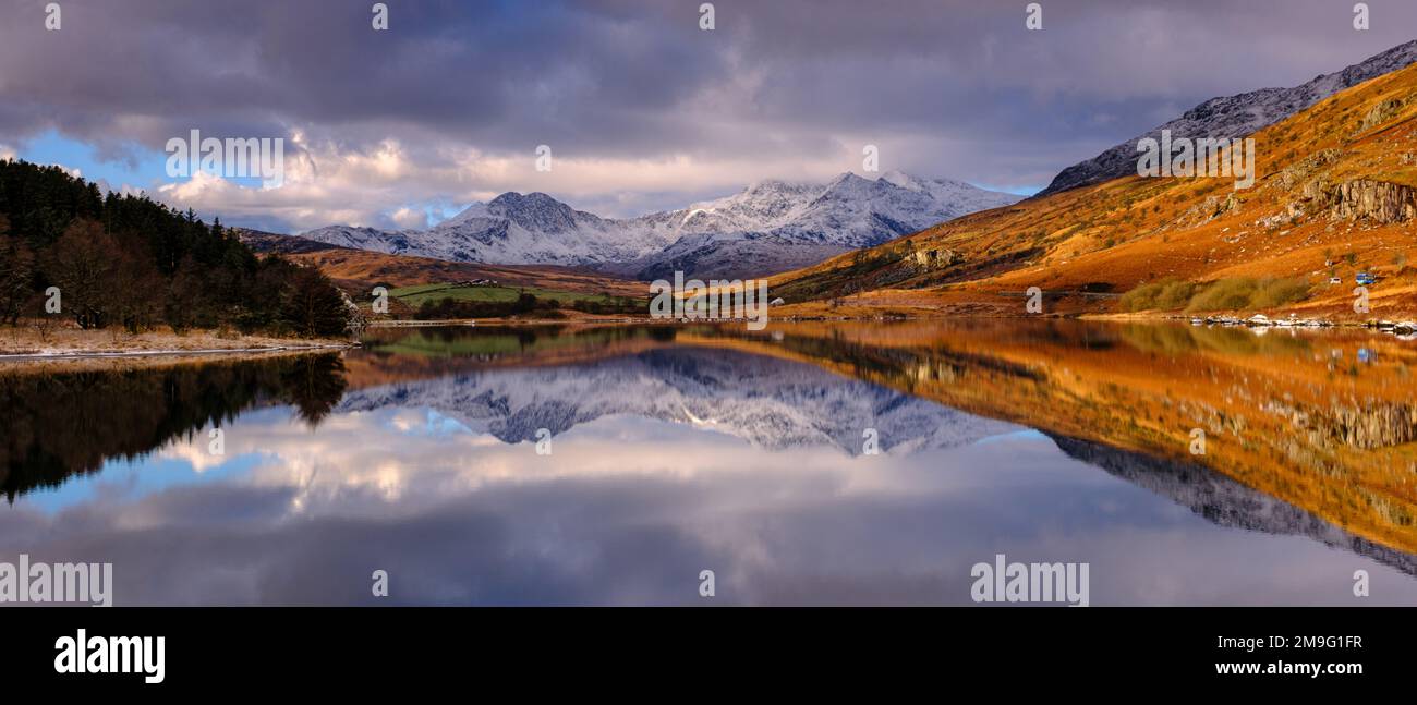 A panoramic view of reflection of snow covered Snowdon Horseshoe mountains in a lake in ...