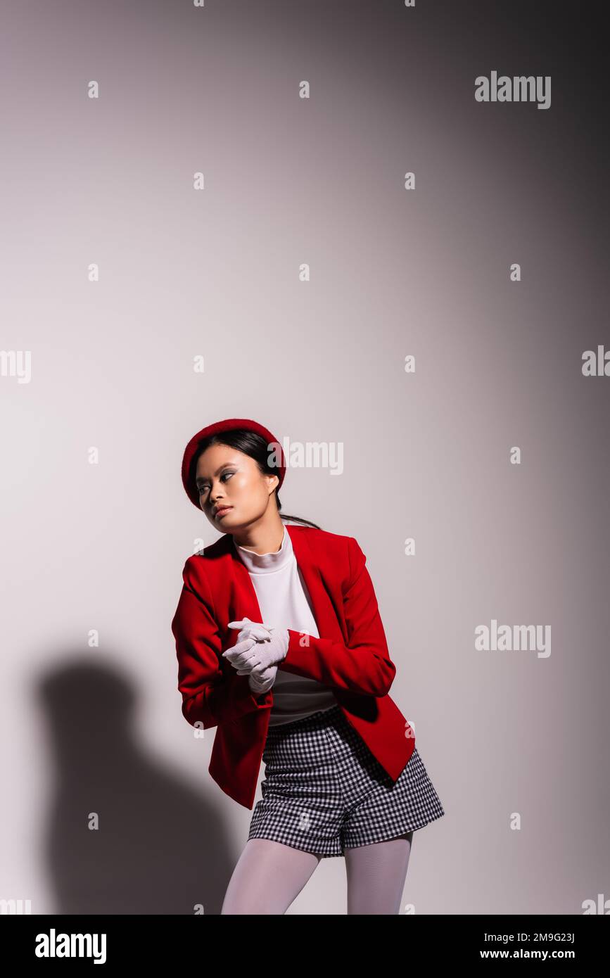 Young asian model in beret and jacket looking away on grey background ...