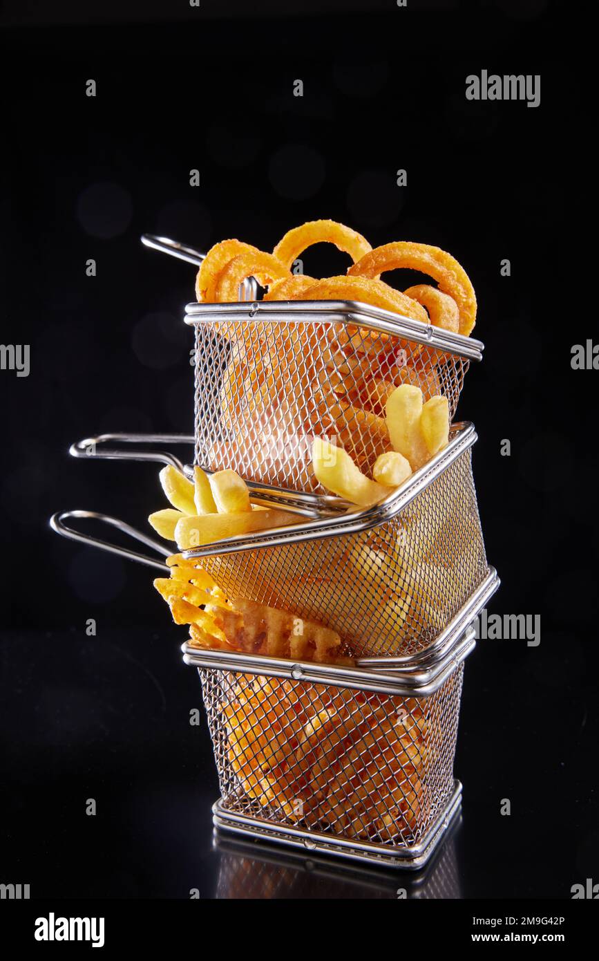 Heap of delicious onion rings with French fries and potato chips served ...