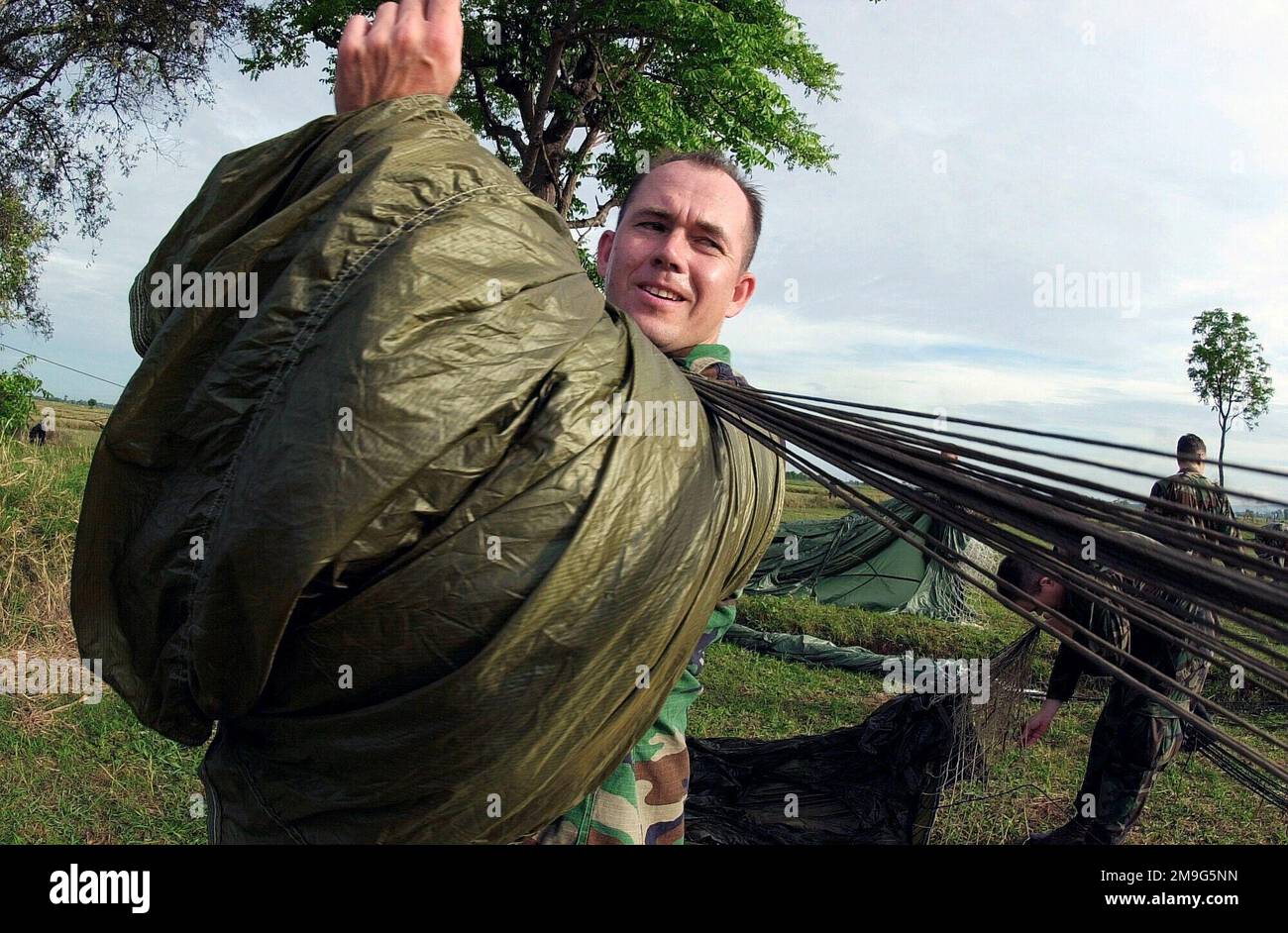 A US Army service member field dresses and stores his parachute after ...