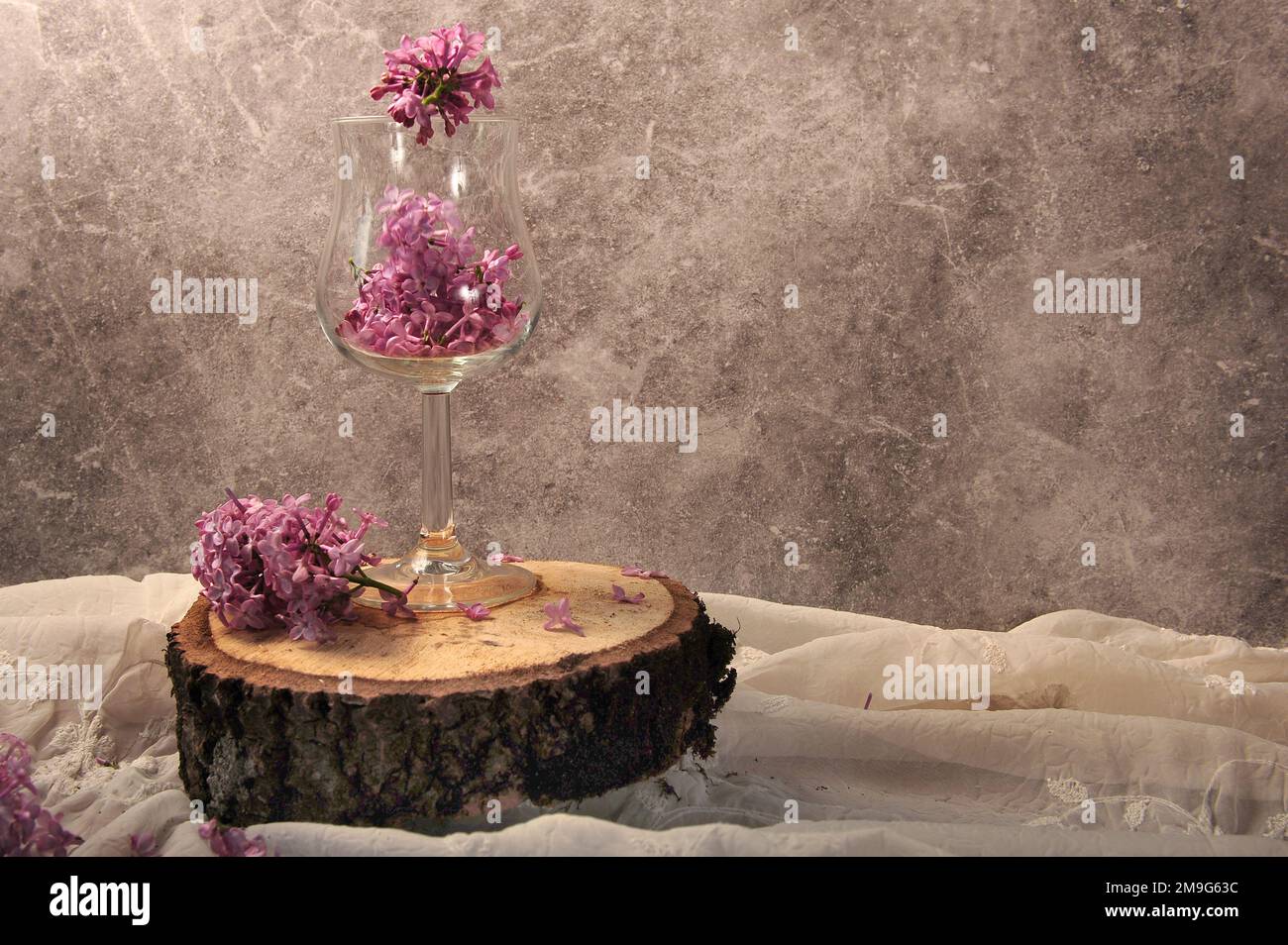 Pink purple lilac flowers in a wine glass placed on slice of tree trunk ...