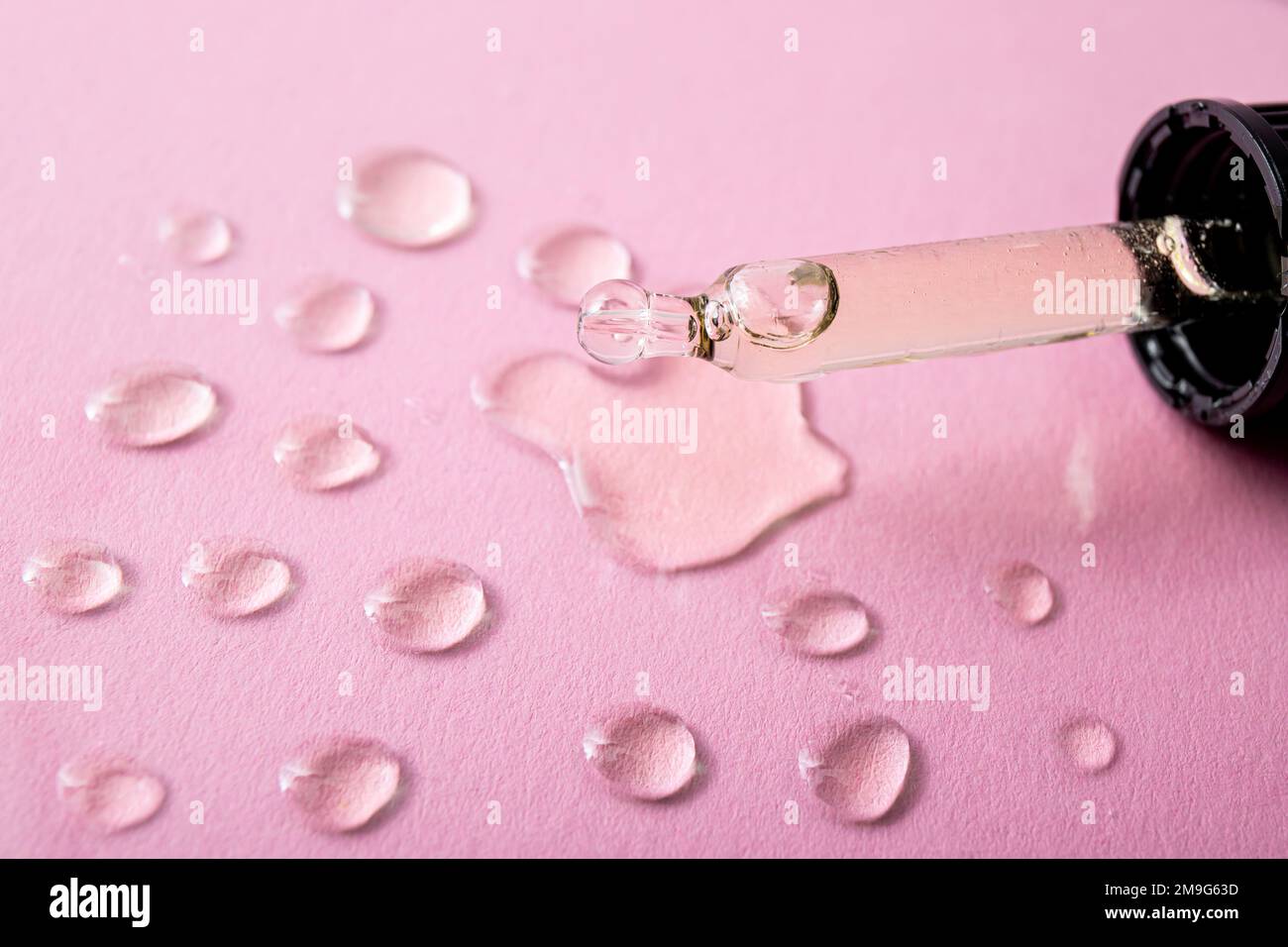 Close up view of glass dropper with oil and oil drops on pink studio ...