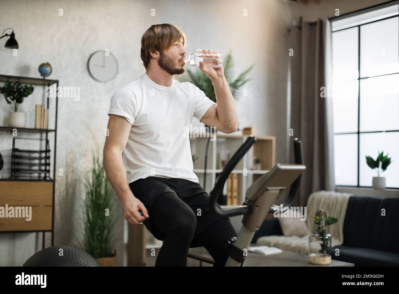 Focused young male wearing sportswear drinking water, using exercise ...