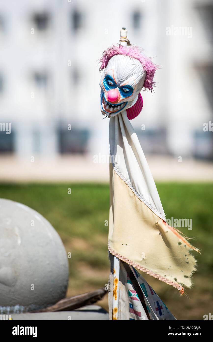 A vertical shot of the creepy mask of a clown on a rusty rod with a ...
