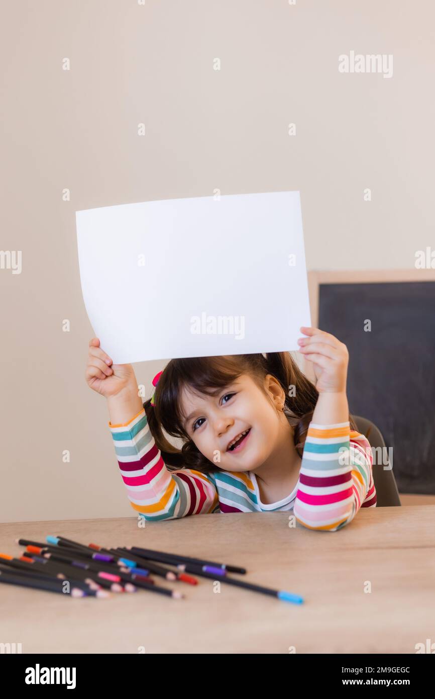 a cute little girl in a drawing lesson holds an empty white sheet in ...