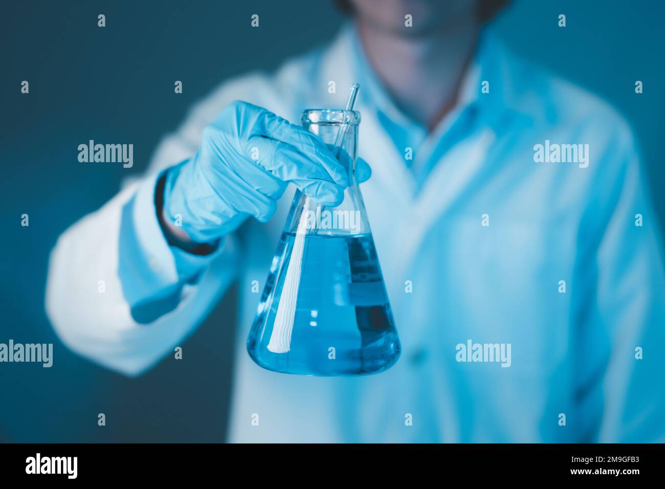 Scientist hand hold erlenmeyer flask with stirring rod filled with blue ...