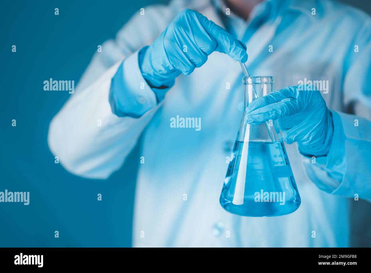 Scientist hand hold erlenmeyer flask with stirring rod filled with blue ...